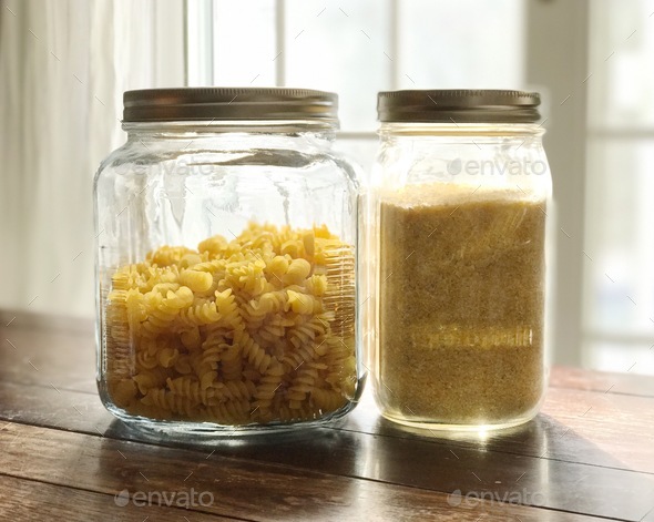Two jars from a pantry with noodles and corn grits on an old wooden ...