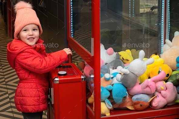 Child, cheerful little girl playing in a vending machine with soft toys ...