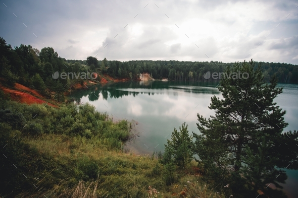 Beautiful blue lake and red clay cliffs in a forest reflecting in a ...