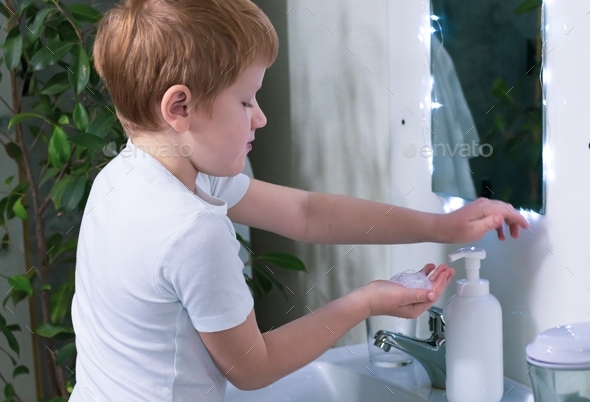 A red-haired teenager boy washing hands in the morning on wash basin ...