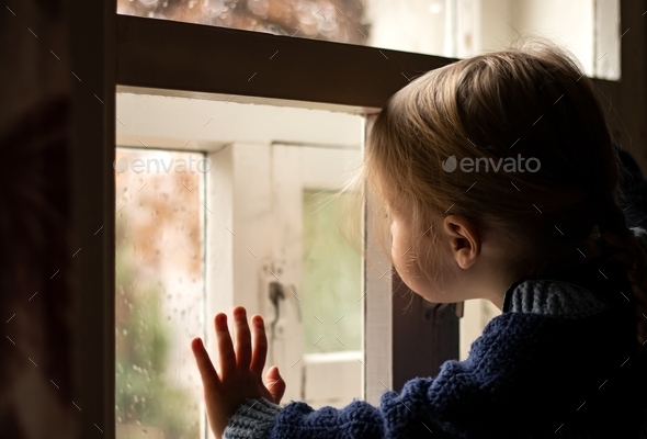 A little girl looks out the window covered with raindrops Stock Photo ...
