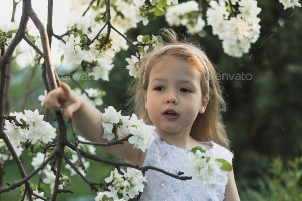 A surprised little girl pointing her finger forward among flowering ...