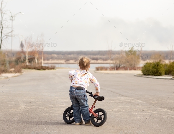 Little girl from behind standing near a running bike looking into the ...