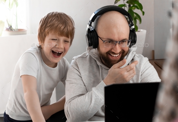 Dad and son having fun, looking at the laptop screen, playing a video ...