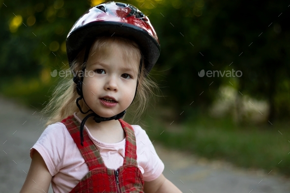Portrait of little girl in red bicycle helmet looking at camera outside ...