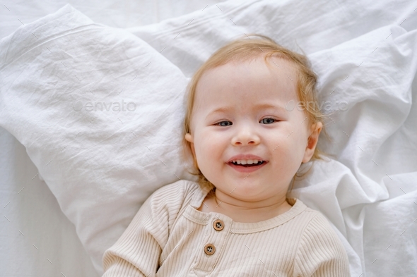 Close up portrait of a cute laughing toddler laying on a bed. Infant ...