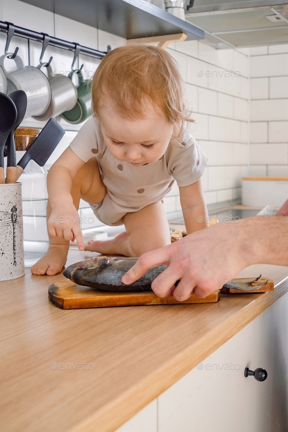A cute toddler surprisingly touching a fish cut cutting by father ...