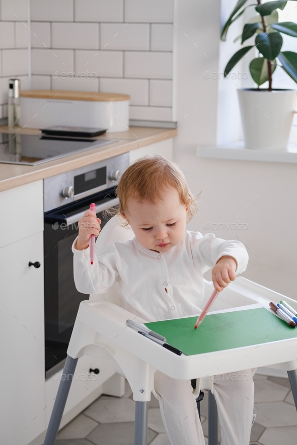 A cute smiling baby toddler sitting on a highchair and drawing first ...