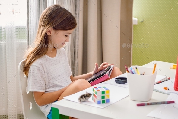 Caucasian school age girl sitting at the messed desk using tablet ...