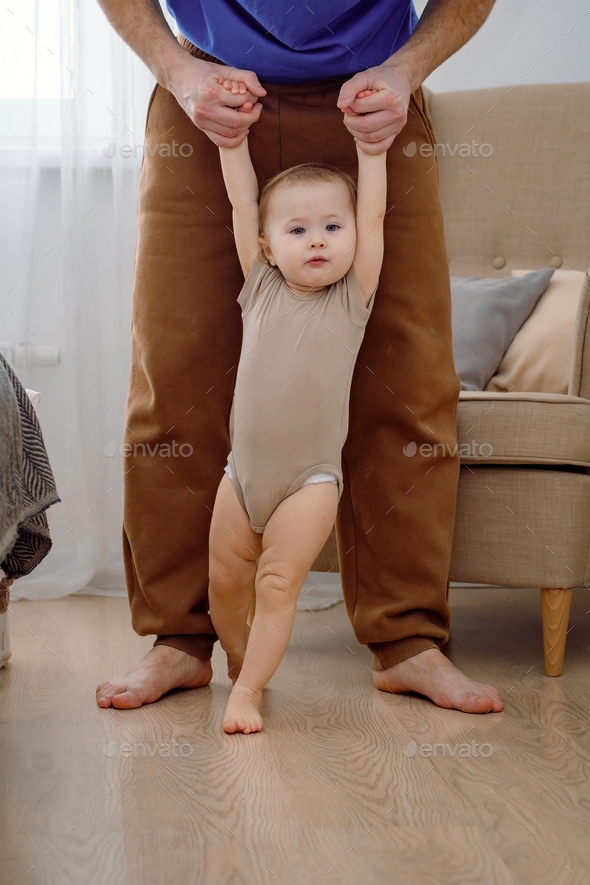 A cute baby trying to make first steps of walking with supported by ...
