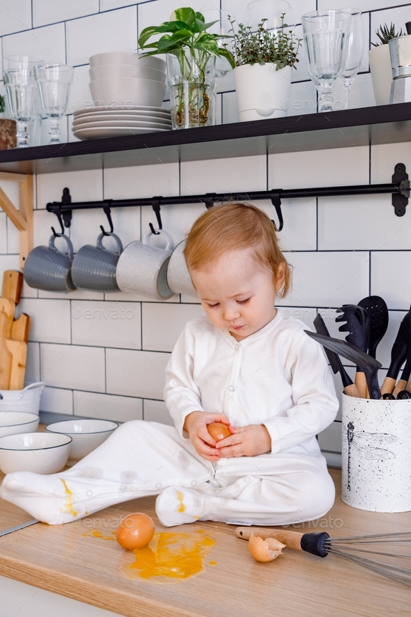 Helping baking a cake. A toddler sitting on the kitchen in mess with ...