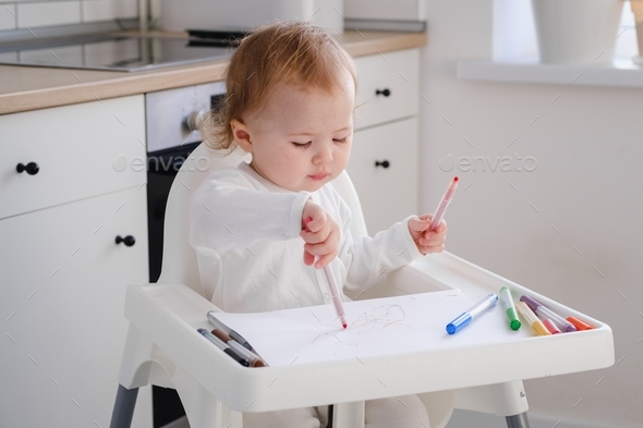 A toddler learning to draw. A baby sitting on a highchair and drawing a ...