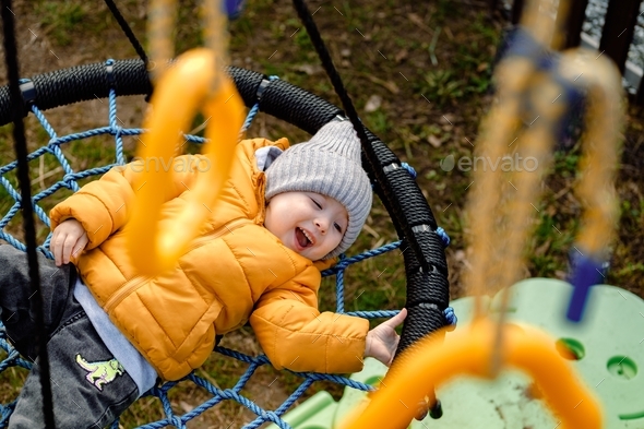 A cute laughing baby have fun swinging in the city park in the spring ...
