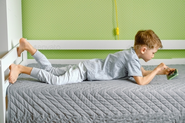 A preschool gen z boy laying on the bed and using mobile phone. Kids ...