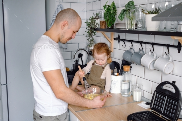 A cute baby toddler mixing ingredients using whisk supported by father ...