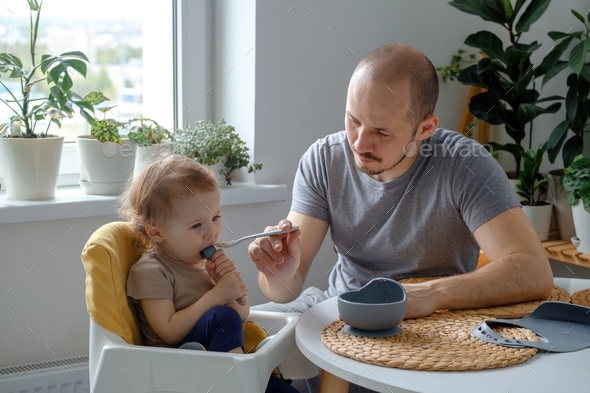 A dad feeding toddler. A cute baby toddler learning self-feeding, a ...