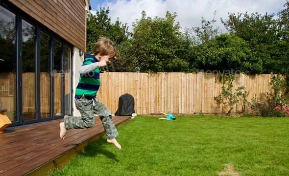 Boy jumping off porch onto lawn in backyard Stock Photo by reinasmyth
