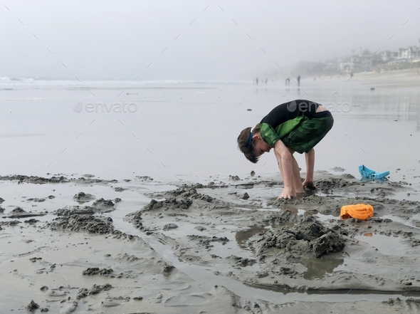 Boy playing and digging in sand at beach on foggy day Stock Photo by ...