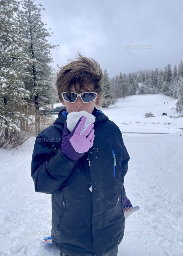 Boy eating snowball on sledding hill Stock Photo by reinasmyth | PhotoDune