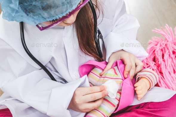 A little caucasian girl in a white coat, a light blue medical cap wipes ...