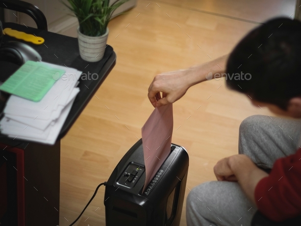 Caucasian young man inserts a sheet of paper for destruction in a black ...