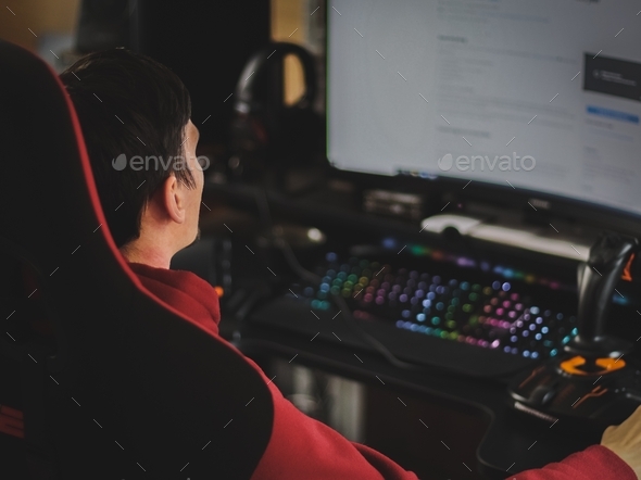 A young caucasian guy sits in a work chair in front of a large computer ...