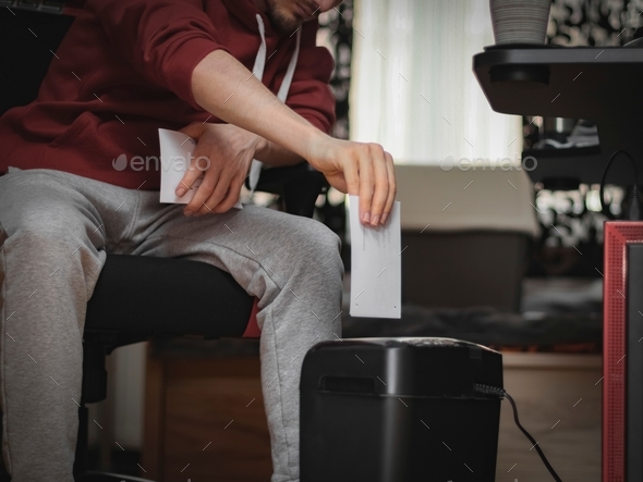 Caucasian young man inserts a sheet of paper for destruction in a black ...