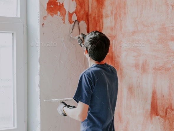 A young handsome caucasian guy putty with fresh putty on the wall near ...