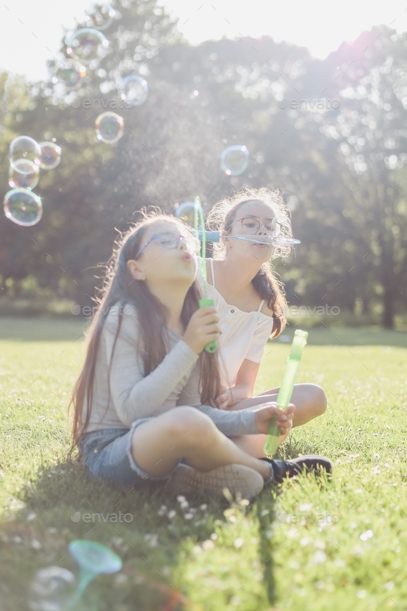 Portrait of two beautiful caucasian girl sisters blow bubbles sitting ...