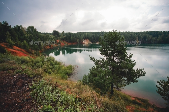 Beautiful blue lake and red clay cliffs in a forest reflecting in a ...