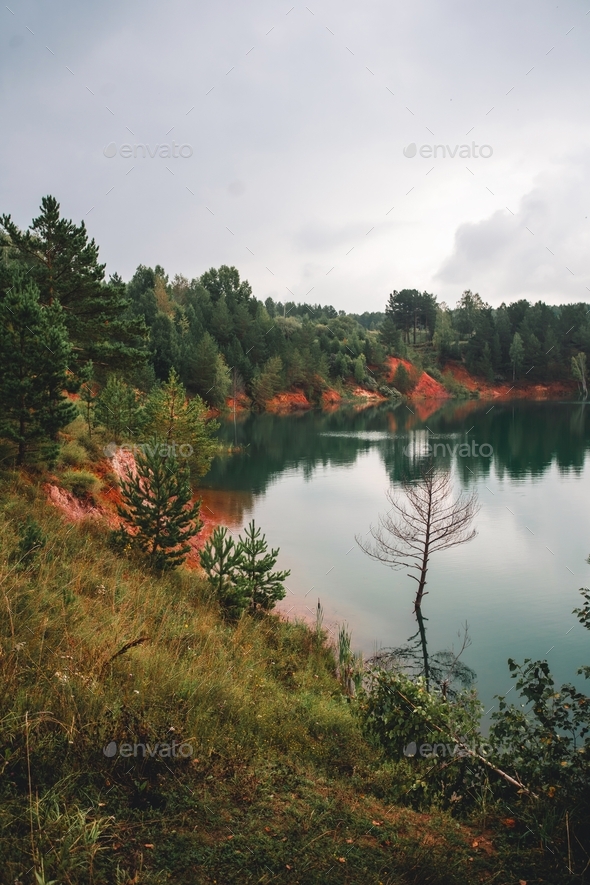 Beautiful blue lake and red clay cliffs in a forest reflecting in a ...