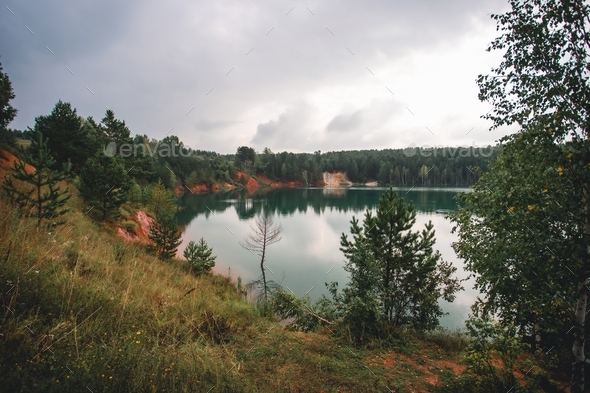 Beautiful blue lake and red clay cliffs in a forest reflecting in a ...