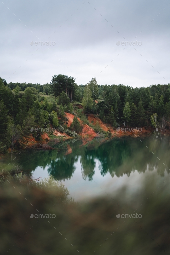 Beautiful blue lake and red clay cliffs in a forest reflecting in a ...