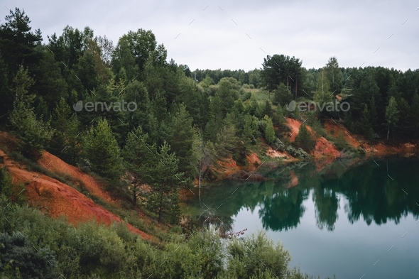 Beautiful blue lake and red clay cliffs in a forest reflecting in a ...