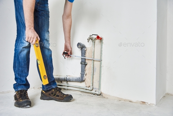 Plumber checks pipe vertical level after installation. Man with level ...