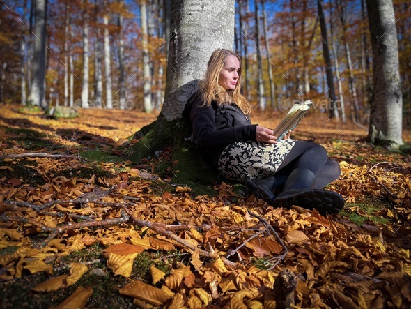 Young woman in the forest during autumn lying down under a tree and ...