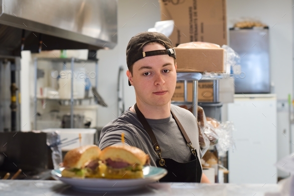 Restaurant kitchen employee placing plate with sandwich food order on ...