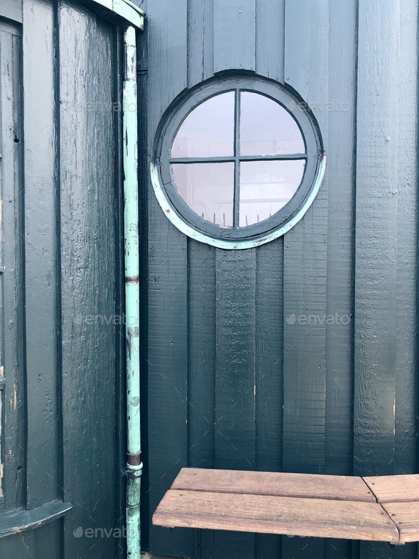 Round window, green wall, and wooden bench Stock Photo by wanaktek