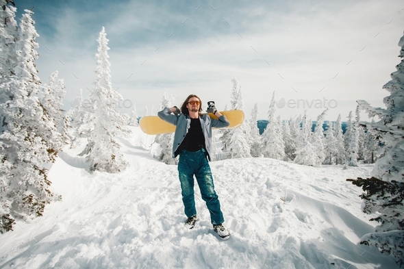 Male snowboarder on a mountain between snowy trees during sunny day ...