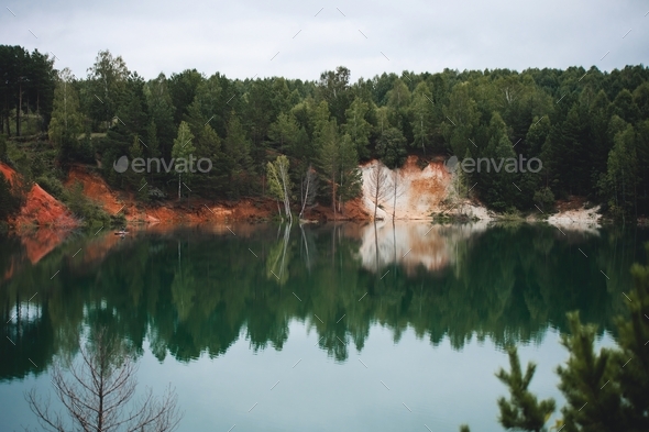 Beautiful blue lake and red clay cliffs in a forest reflecting in a ...