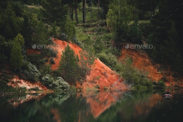 Beautiful blue lake and red clay cliffs in a forest reflecting in a ...