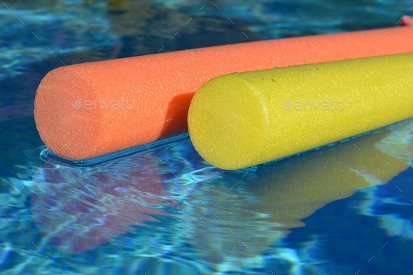 Orange and yellow pool noodles floating in sparkling blue swimming pool ...