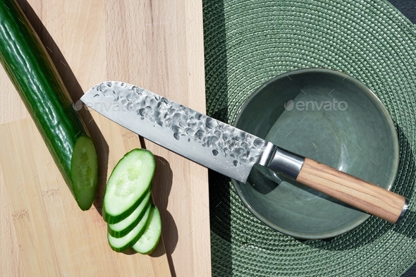 Sharp chef's knife close up on the cutting board and sliced cucumber ...