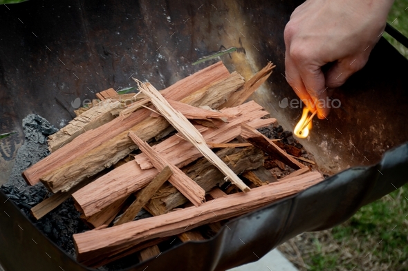 Hand holding a safety match starting the camp fire with kindling in a ...