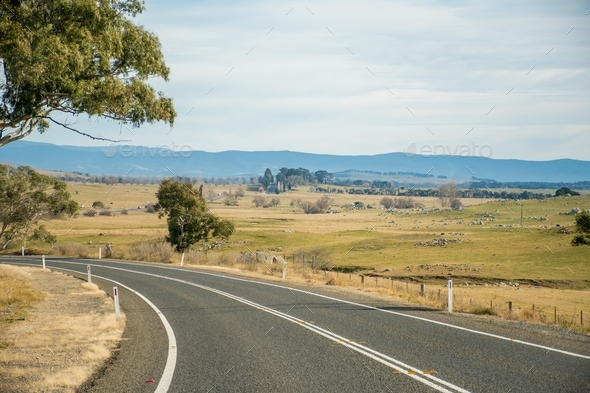 Open empty road surrounded by fields and farms in Australia. Mountains ...