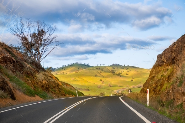 Open empty road surrounded by green hills, fields and farms in ...