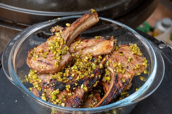 Lamb cutlets grilled on bbq grill in a glass bowl with pistachio nuts ...