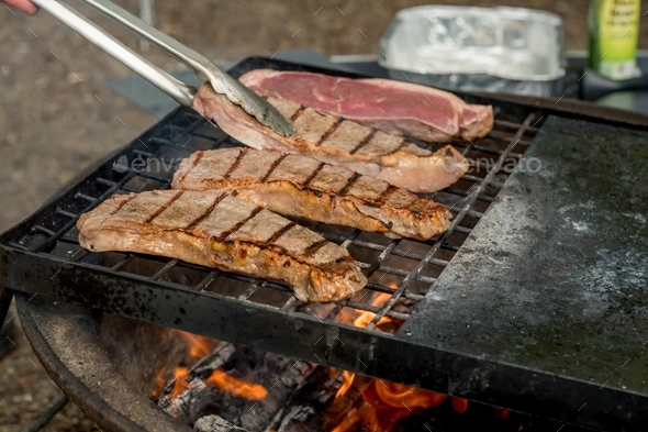 BBQ grilling meat beef steaks on a cast iron plate over campfire ...