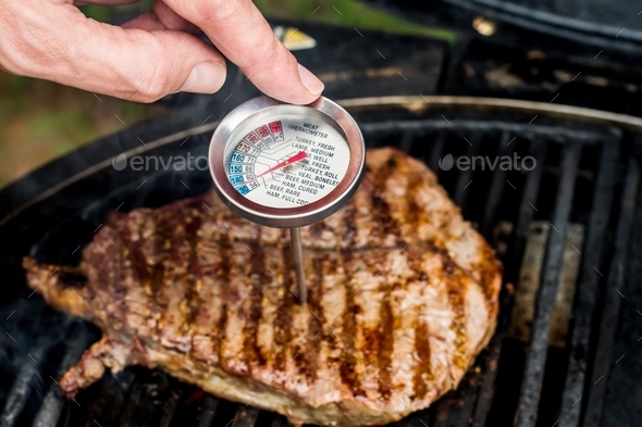 Grilled meat on bbq with hand holding meat cooking thermometer to check ...