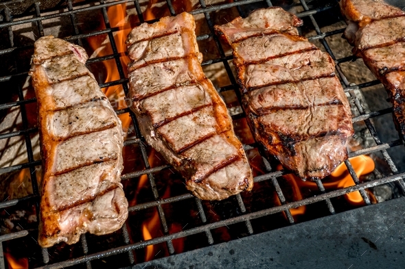 BBQ grilling meat beef steaks on a cast iron grill over the campfire ...